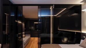 Quarto de hotel moderno com cama, área de estar, cozinha compacta e uma grande janela.
