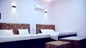 Quarto de hotel com duas camas, um sofá, uma mesinha e um aparelho de ar condicionado.