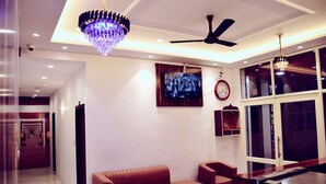 Um hall de hotel moderno com um candelabro, ventoinha no teto, televisão, relógio e área de estar.