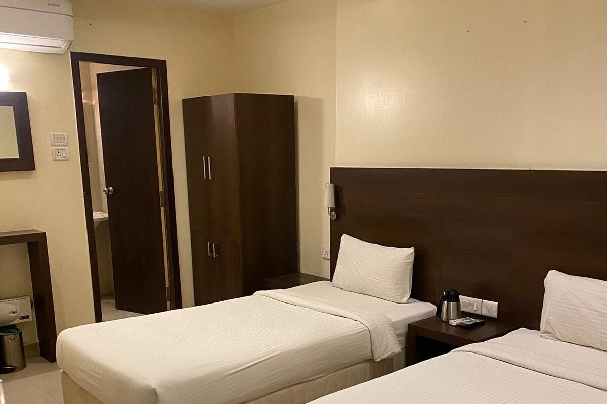 Quarto de hotel com duas camas, um guarda-roupa, uma mesa de cabeceira e um espelho.