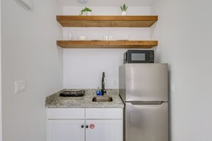 Uma cozinha compacta com geladeira de aço inoxidável, micro-ondas, pia e prateleiras de madeira acima.