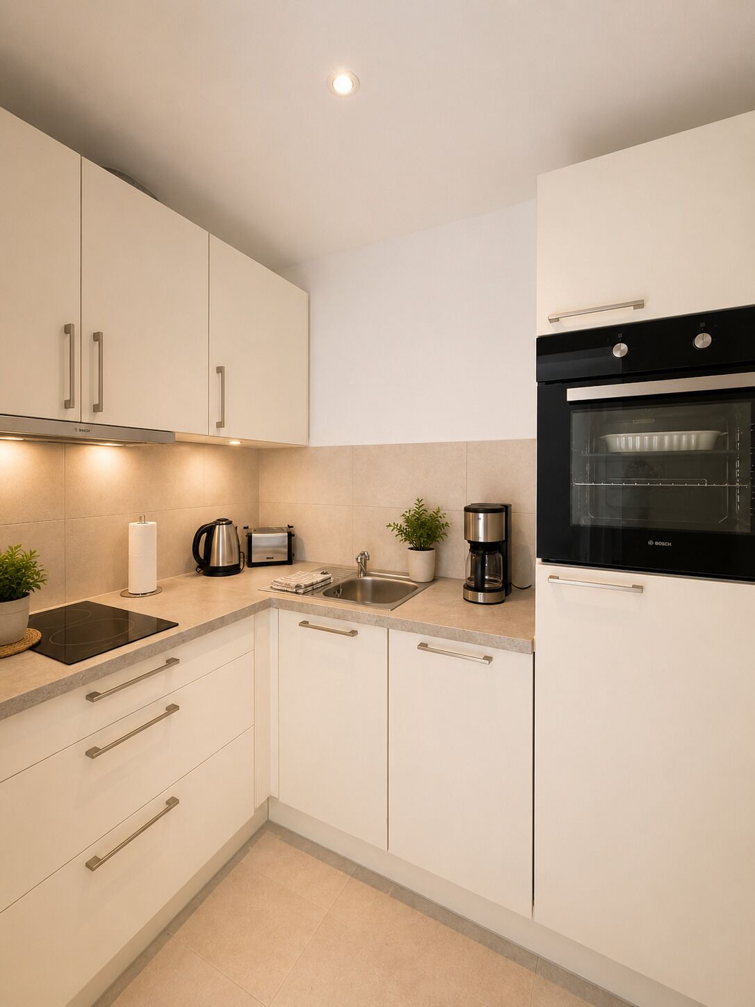 Uma cozinha moderna com armários brancos, forno Bosch, cafeteira e torradeira.
