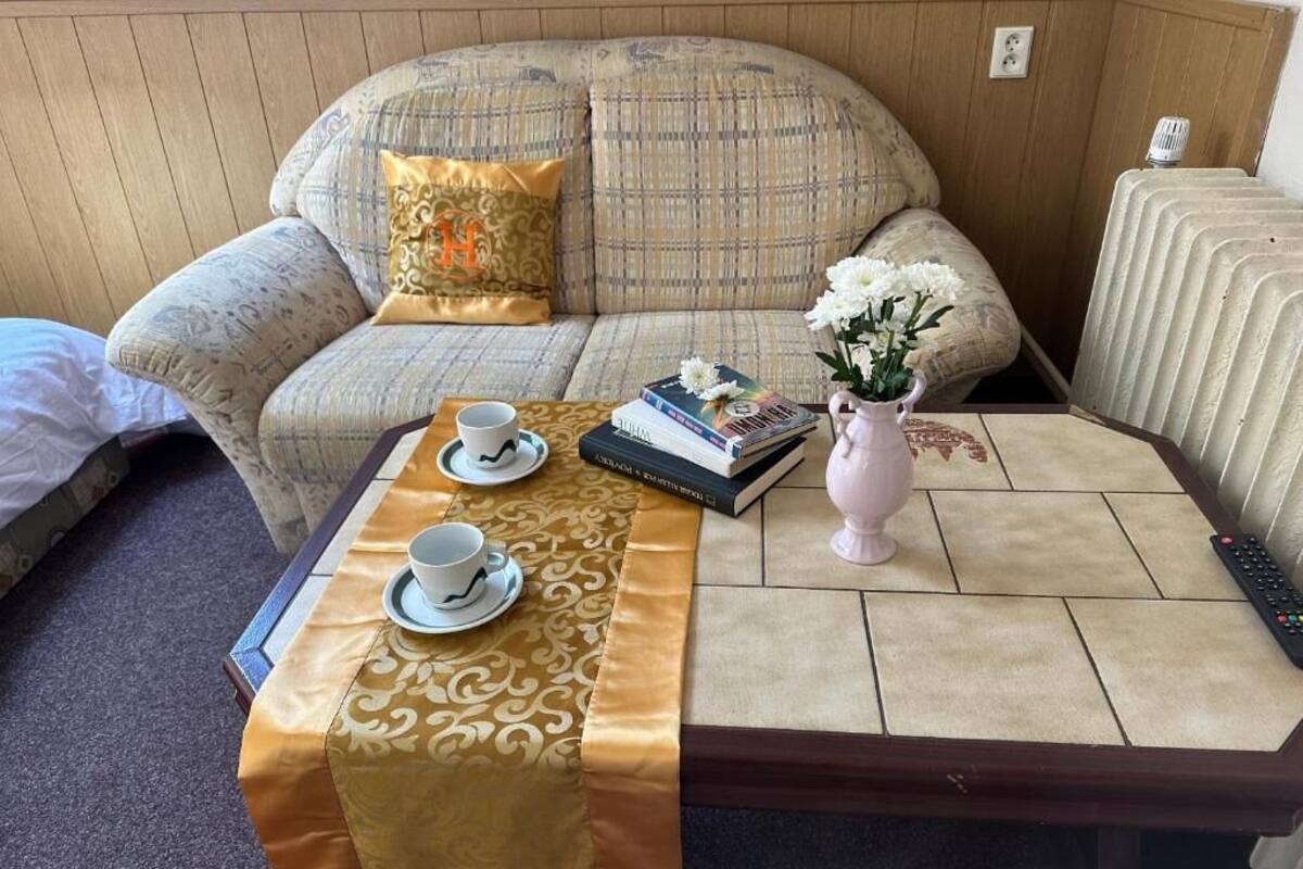 Quarto com sofá, mesa de centro com um vaso de flores, controle remoto e um livro.