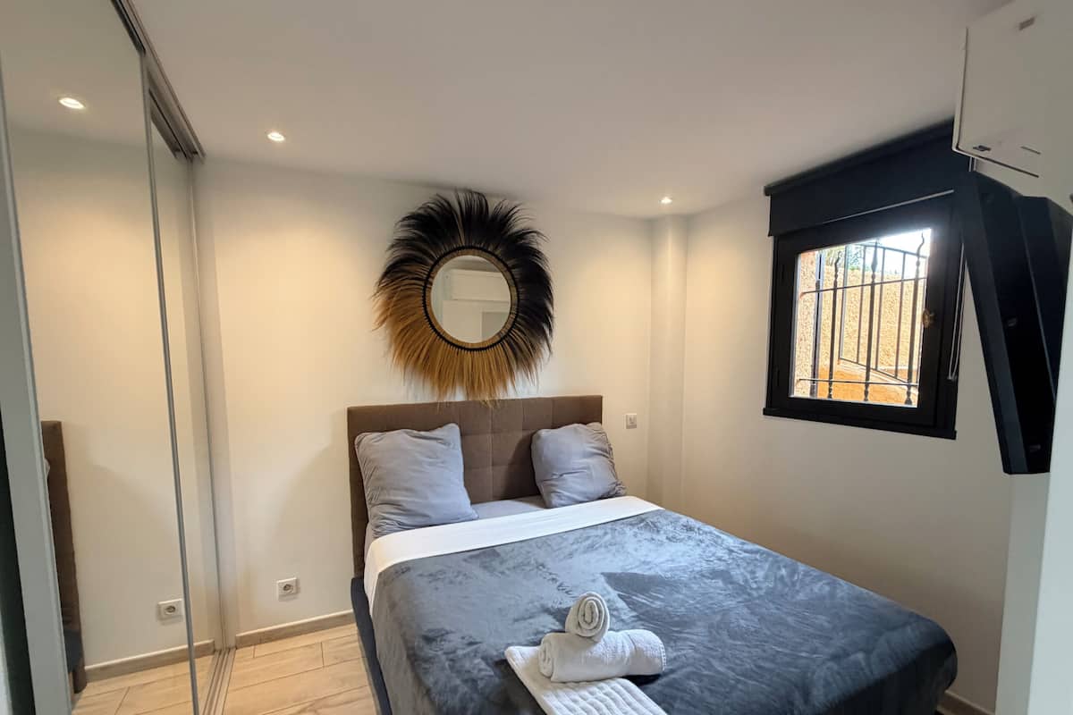 Quarto com cama, espelho redondo, janela e ventilador de teto.