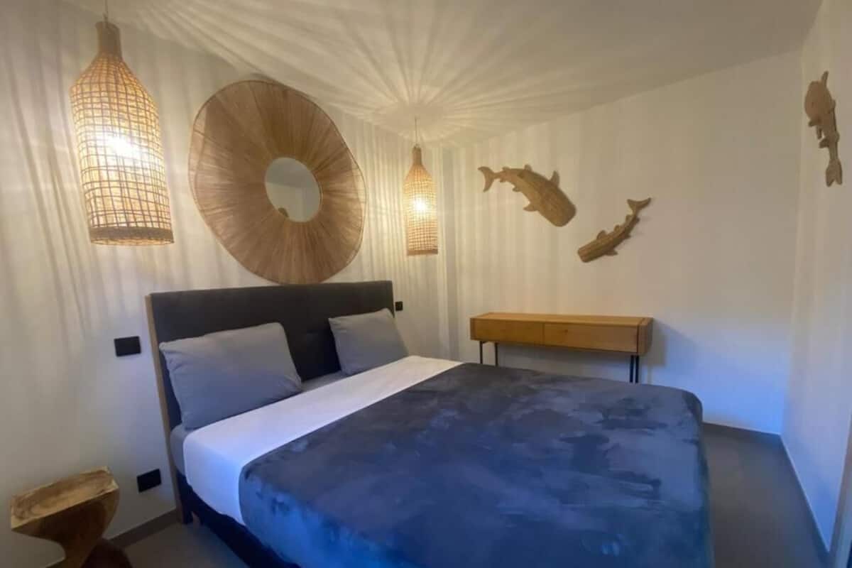 Quarto com cama, mesas de cabeceira, luminária pendente e decoração na parede.