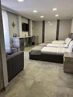 Quarto de hotel moderno com sofá, duas camas, escrivaninha e televisão.