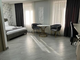 Quarto de hotel com uma cama, duas poltronas, uma mesa redonda e um painel decorativo na parede.