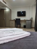 Quarto com cama, escrivaninha, cadeira, televisão e um pequeno frigorífico.