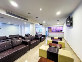 Um hall de hotel com sofás de couro, área de bar e uma televisão na parede.