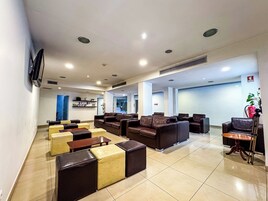Um saguão de hotel com sofás de couro, mesas de madeira e um balcão de recepção.