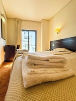 Quarto de hotel com cama, mesa de cabeceira, abajur, janela com cortinas e vista para o exterior.