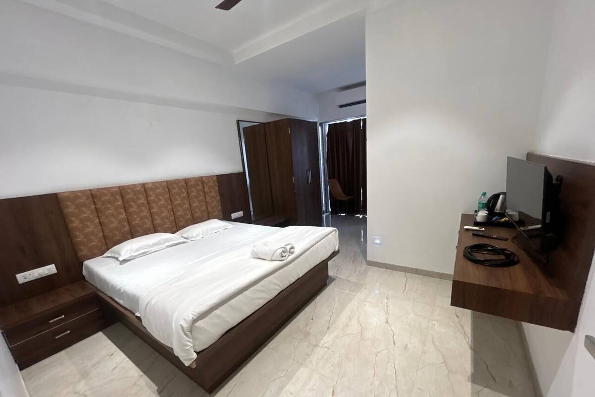 Quarto de hotel com cama, televisão, escrivaninha e guarda-roupa.