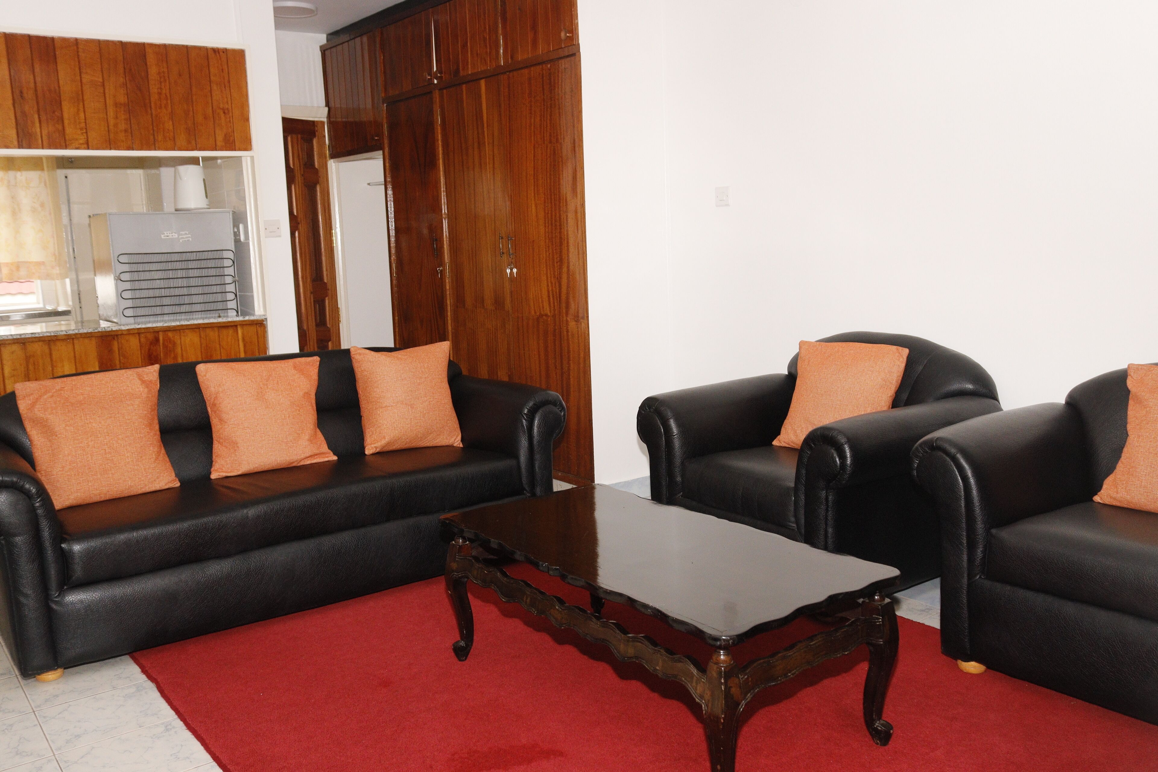 Uma sala de estar com um sofá de couro preto, uma mesa de centro de madeira e um tapete vermelho.
