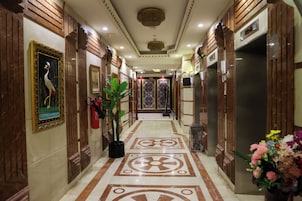 Um corredor com piso de mármore, painéis de madeira, um quadro emoldurado, uma planta em vaso e um elevador.
