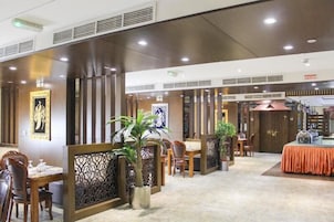 Um saguão de hotel com balcão de recepção, área de estar e plantas decorativas.