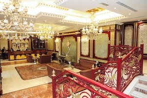 Um hall luxuoso com lustres, uma escadaria imponente e áreas de estar confortáveis.