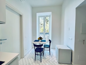 Uma cozinha pequena com uma mesa de jantar, duas cadeiras, uma geladeira e uma janela com vista para árvores.