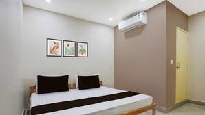 Quarto de hotel com cama, mesa de cabeceira, aparelho de ar condicionado e três quadros na parede.