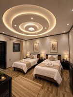 Quarto de hotel com duas camas, luminária circular no teto e piso de madeira.