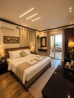 Quarto de hotel moderno com uma cama grande, mesas de cabeceira, uma escrivaninha e vista para o exterior.