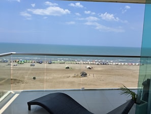 Uma varanda com vista para a praia, uma cadeira de descanso e um vaso de planta.