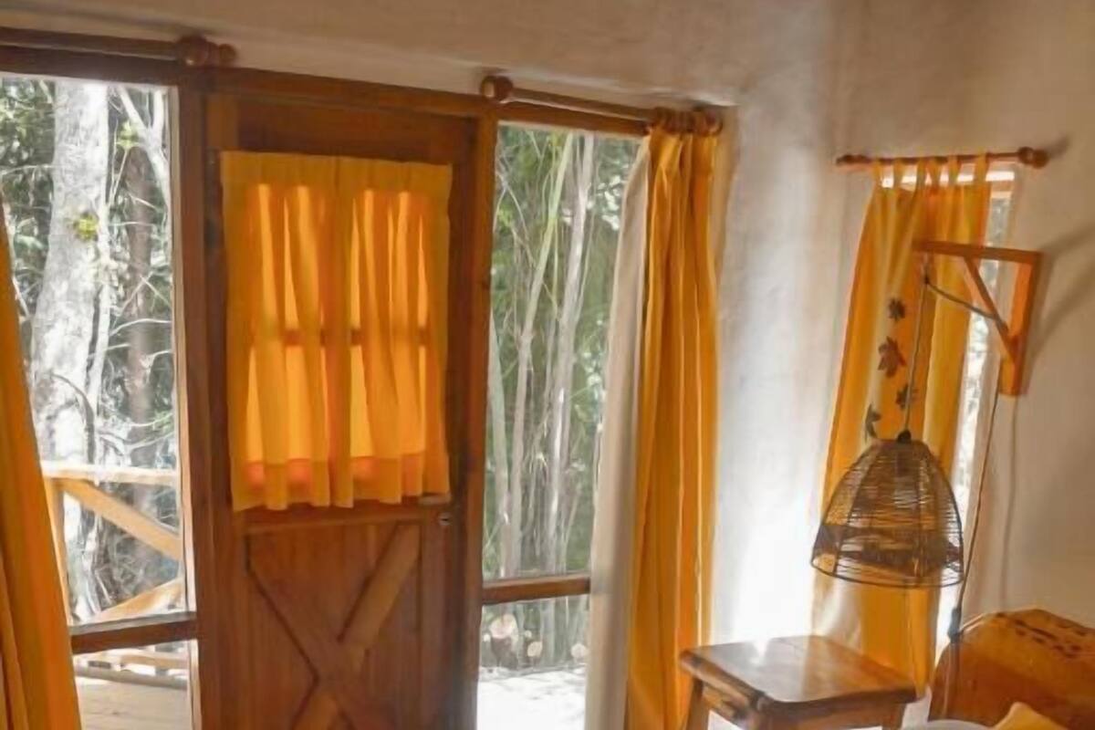 Quarto com cama, porta de madeira, mesa pequena e luminária suspensa.