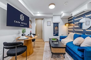 Uma sala de estar moderna com um sofá azul, uma mesa de jantar de madeira e uma TV montada exibindo 'CASA HOTELS TORONTO'.