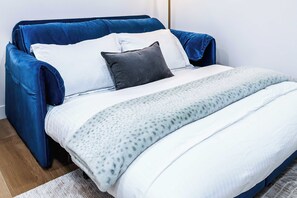 Uma cama com cabeceira azul, almofadas brancas e cinzentas escuras e um cobertor estampado.