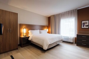 Quarto de hotel com cama, mesas de cabeceira, guarda-roupa, radiador e janela com cortinas.