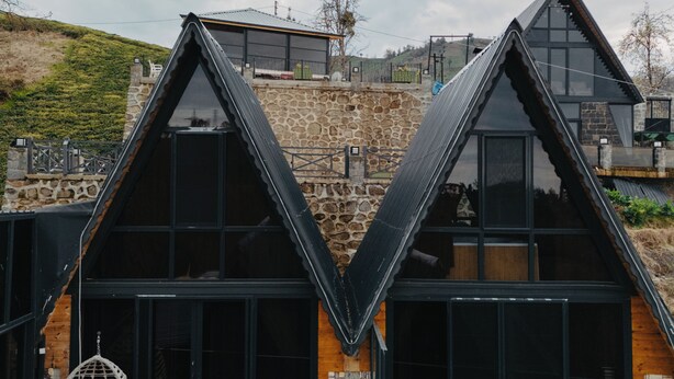 Um edifício moderno com fachada de pedra e grandes janelas, apresentando um pátio com cadeiras e mesas.