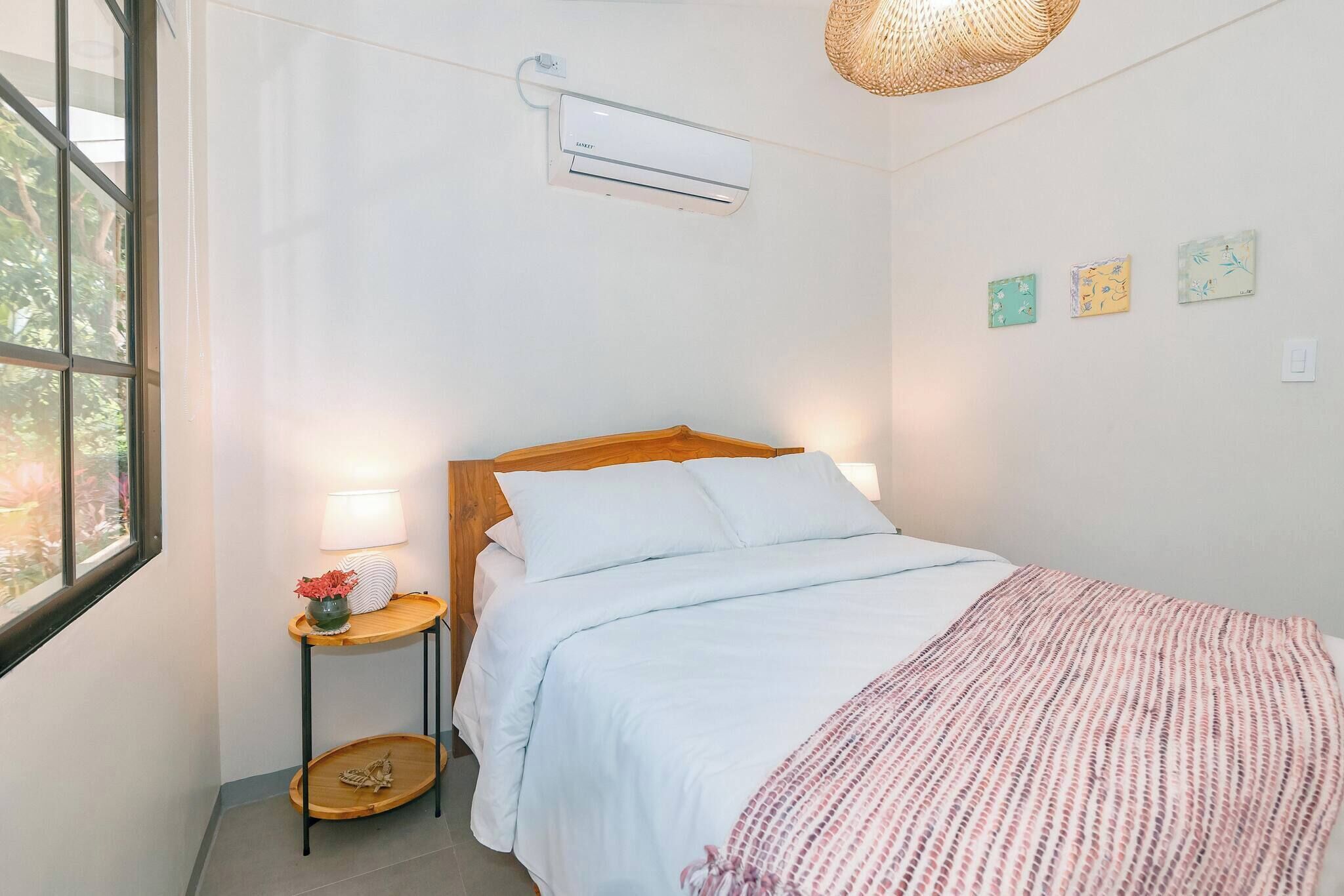 Quarto com cama, mesa de cabeceira, luminária, aparelho de ar condicionado e obra de arte na parede.