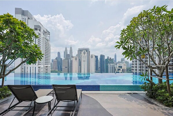 Piscina infinita no terraço com espreguiçadeiras, rodeada por vegetação, com vista para o horizonte urbano.