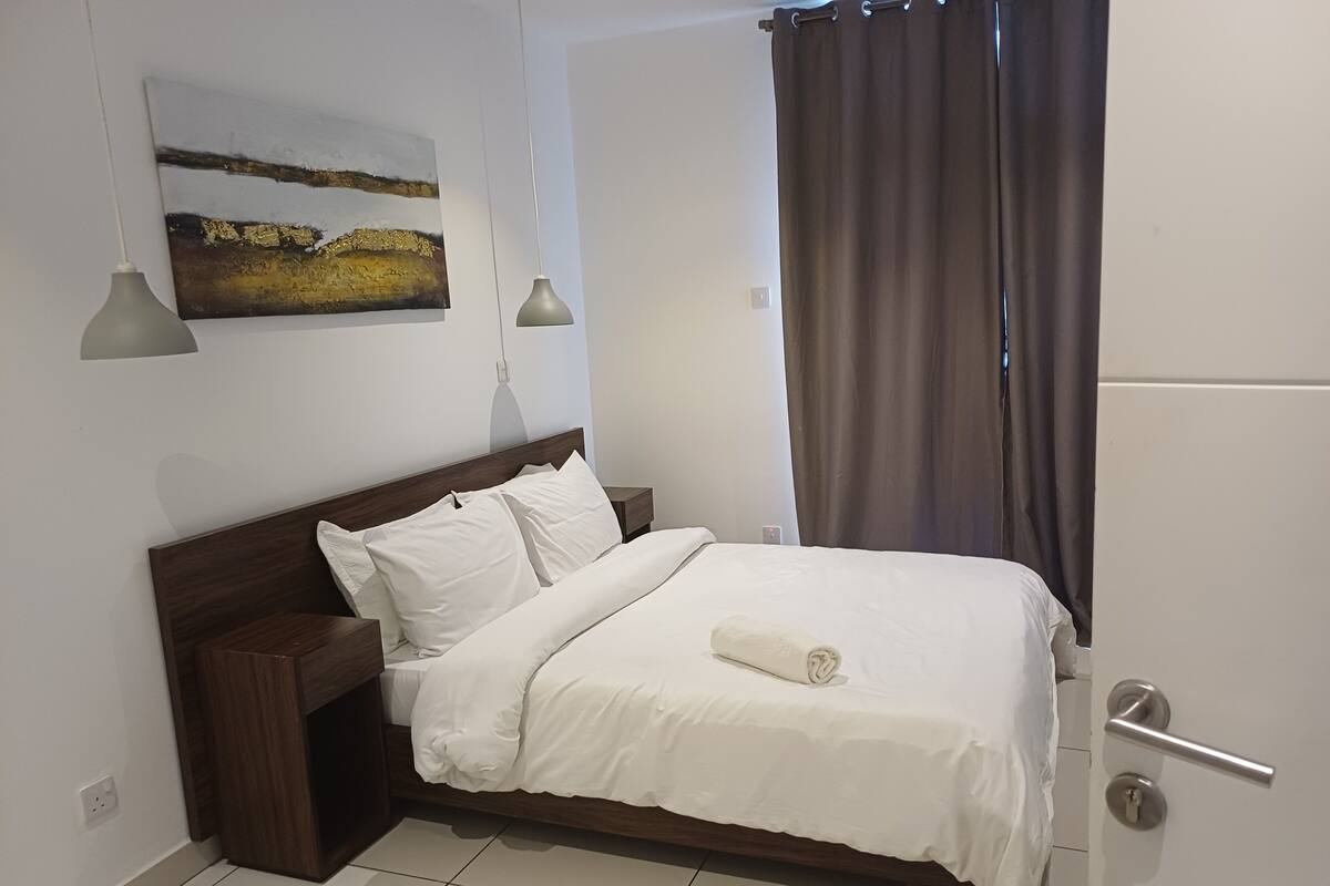 Cama bem arrumada com lençóis brancos, cabeceira de madeira e um único travesseiro branco.