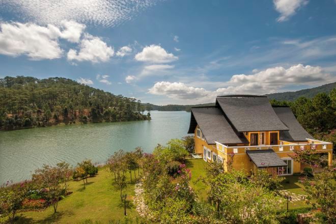 Uma casa com telhado inclinado, com vista para um lago, rodeada por vegetação.