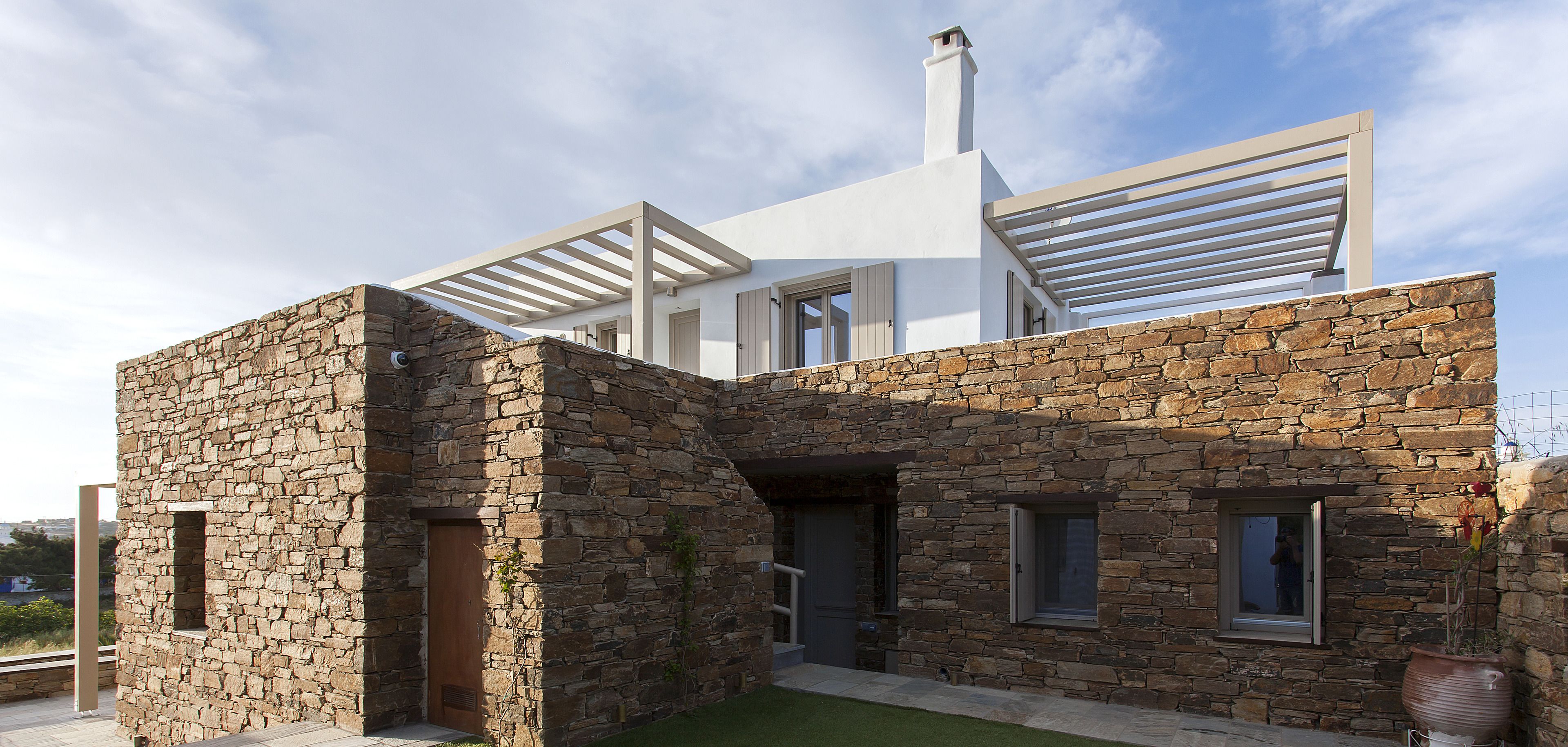 Uma casa moderna com paredes de pedra, fachada branca e pérgula.