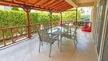 Uma área externa coberta com mesa e cadeiras de vidro, cercada por um guarda-corpo de metal.