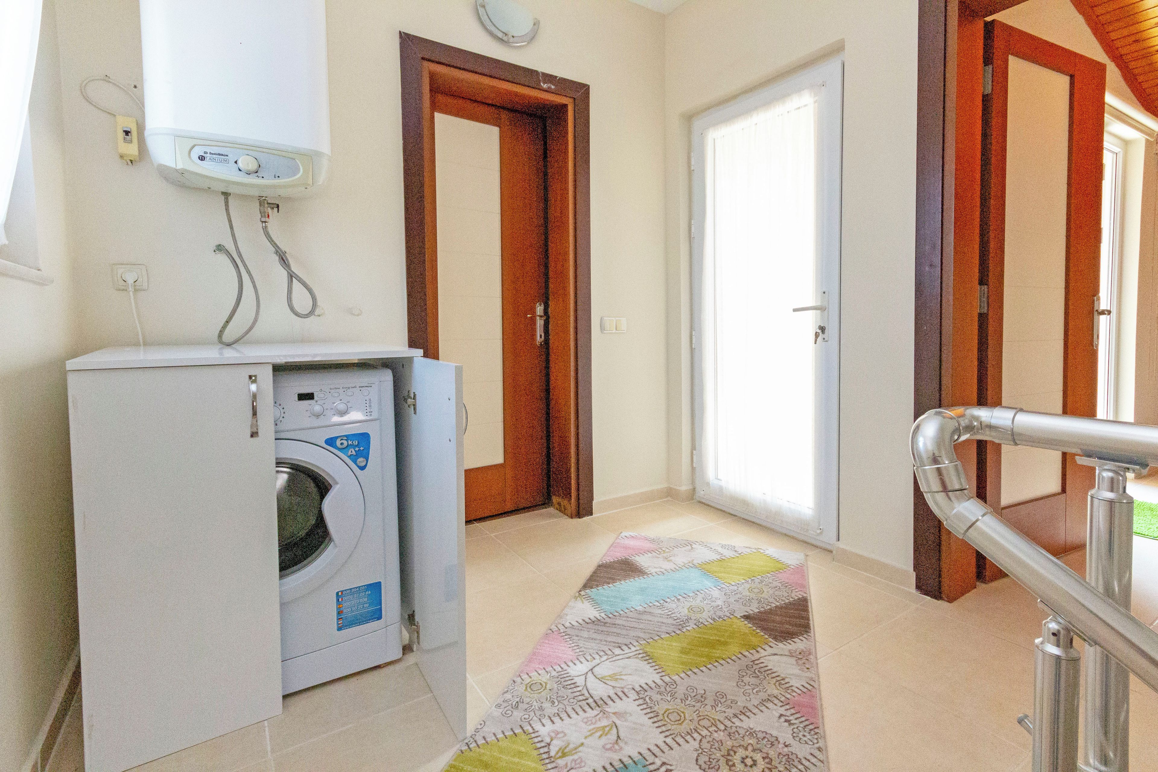 Uma lavanderia com máquina de lavar, porta de madeira e chão de azulejos.