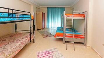 Quarto tipo dormitório com beliches, tapete listrado e cortina azul.