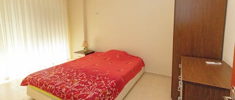 Quarto com cama, guarda-roupa de madeira, mesa de cabeceira e abajur.