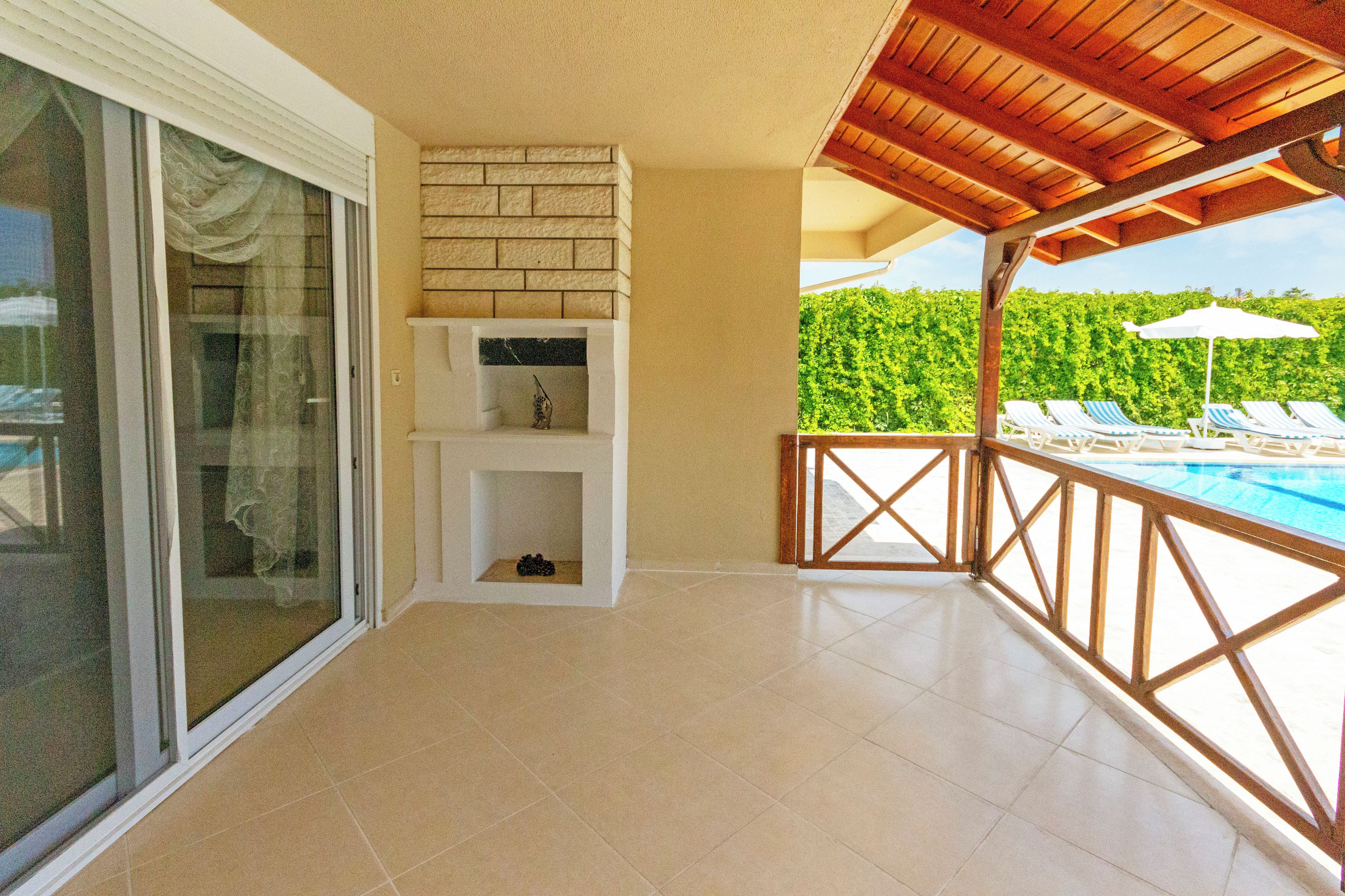 Uma varanda com piscina, espreguiçadeiras e vista para o verde.
