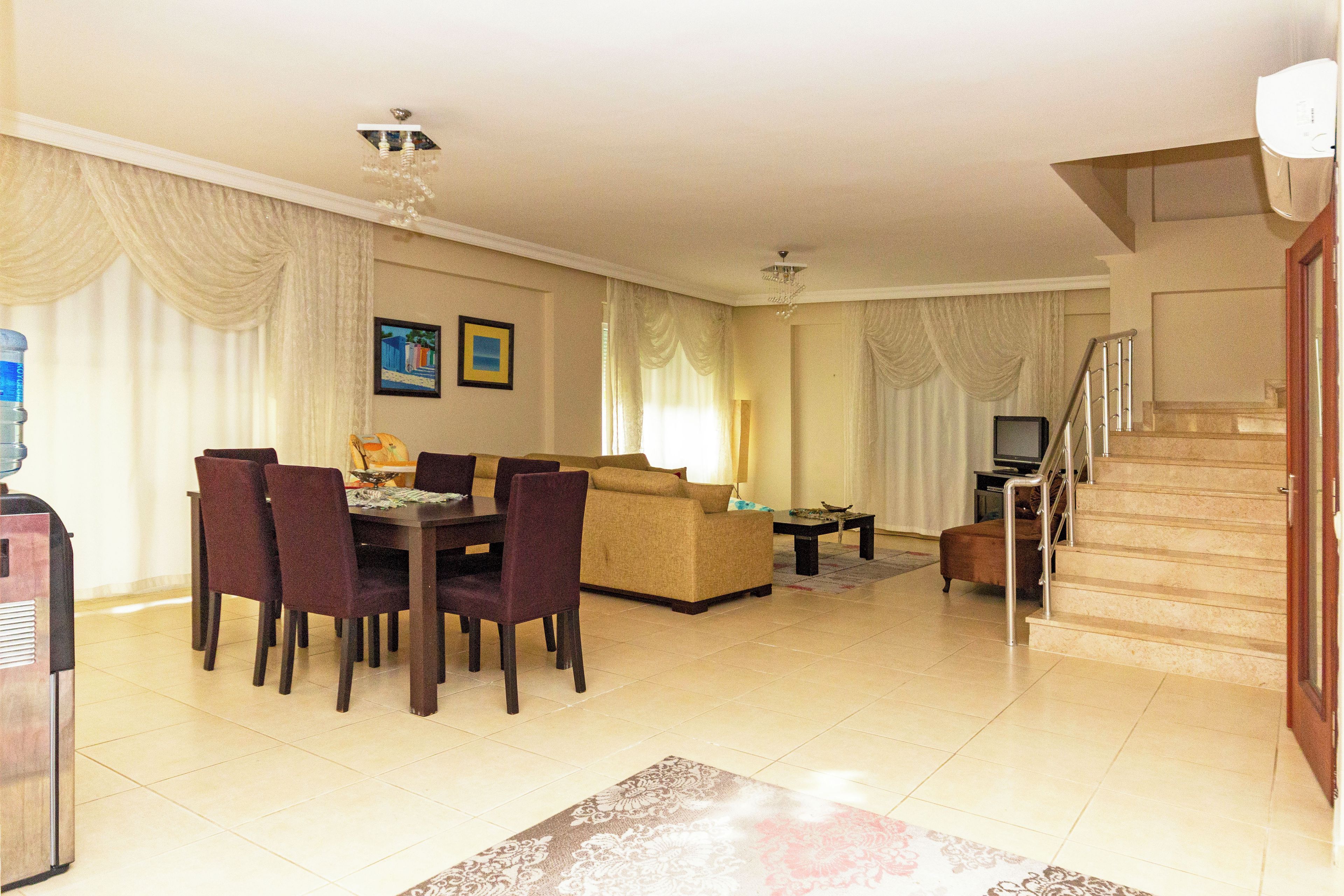 Uma sala de estar ampla com área de jantar, escada e um bebedouro.