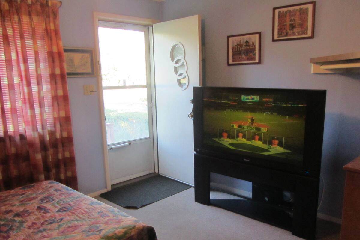 Quarto de hotel com cama, televisão, porta e janela.
