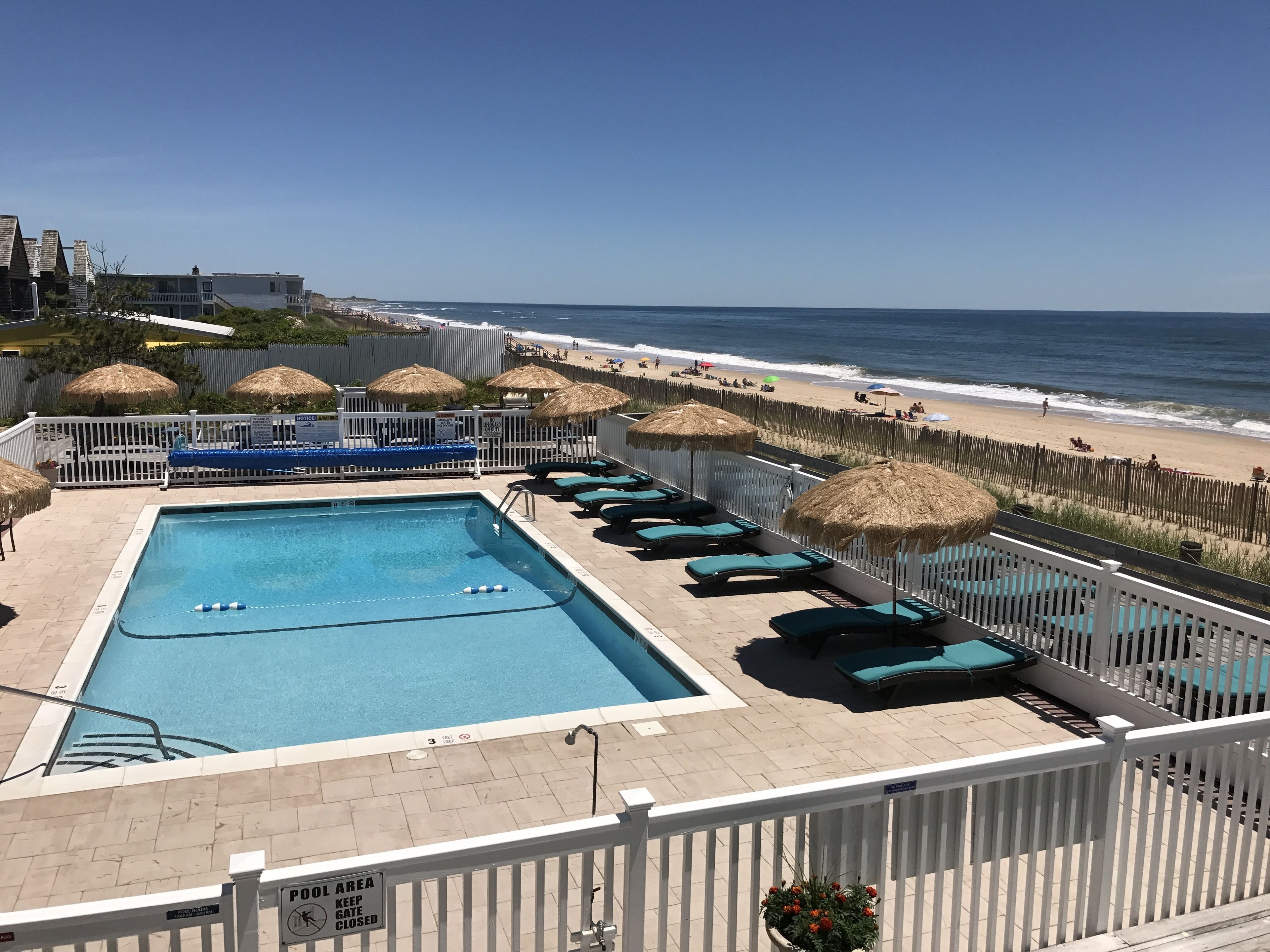 Piscina no terraço com cadeiras de sol e guarda-sóis, com vista para a praia.