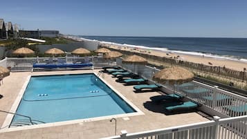 Piscina no terraço com cadeiras de sol e guarda-sóis, com vista para a praia.