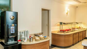 Uma área de recepção de hotel com uma máquina de café, um buffet e um abajur fixado na parede.