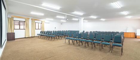 Uma sala de conferências com fileiras de cadeiras, um projetor e um púlpito.