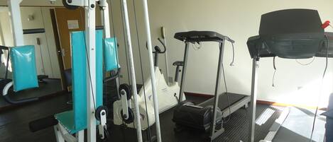 Academia com equipamentos de ginástica, incluindo esteira, aparelhos de musculação e bicicleta ergométrica.