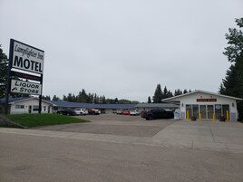 Um motel com uma loja de bebidas, vários veículos estacionados e um edifício com uma placa.