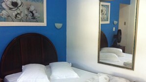 Cama bem arrumada com roupa de cama e toalhas brancas, cabeceira de madeira e um espelho grande na parede.