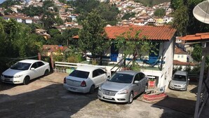 Uma área de estacionamento com três carros, um edifício com telhado vermelho e uma área residencial arborizada ao fundo.